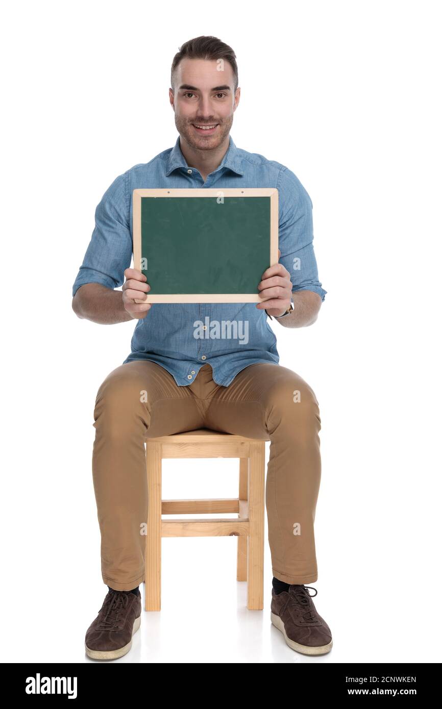 Happy smart casual man smiling and holding blackboard while sitting on ...