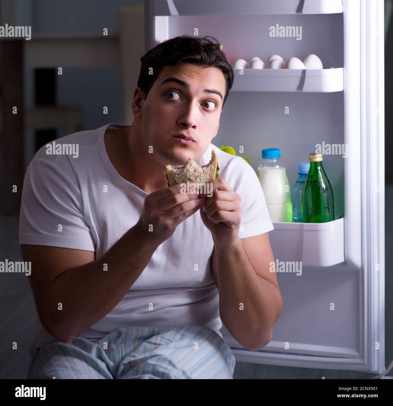 Man at the fridge eating at night Stock Photo - Alamy