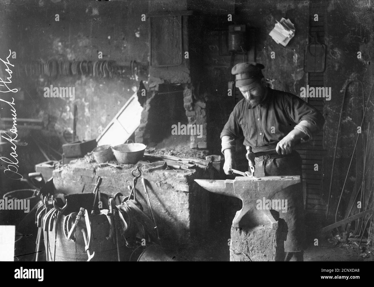 Blacksmith hammering on an anvil next to a brick oven with tools and ...