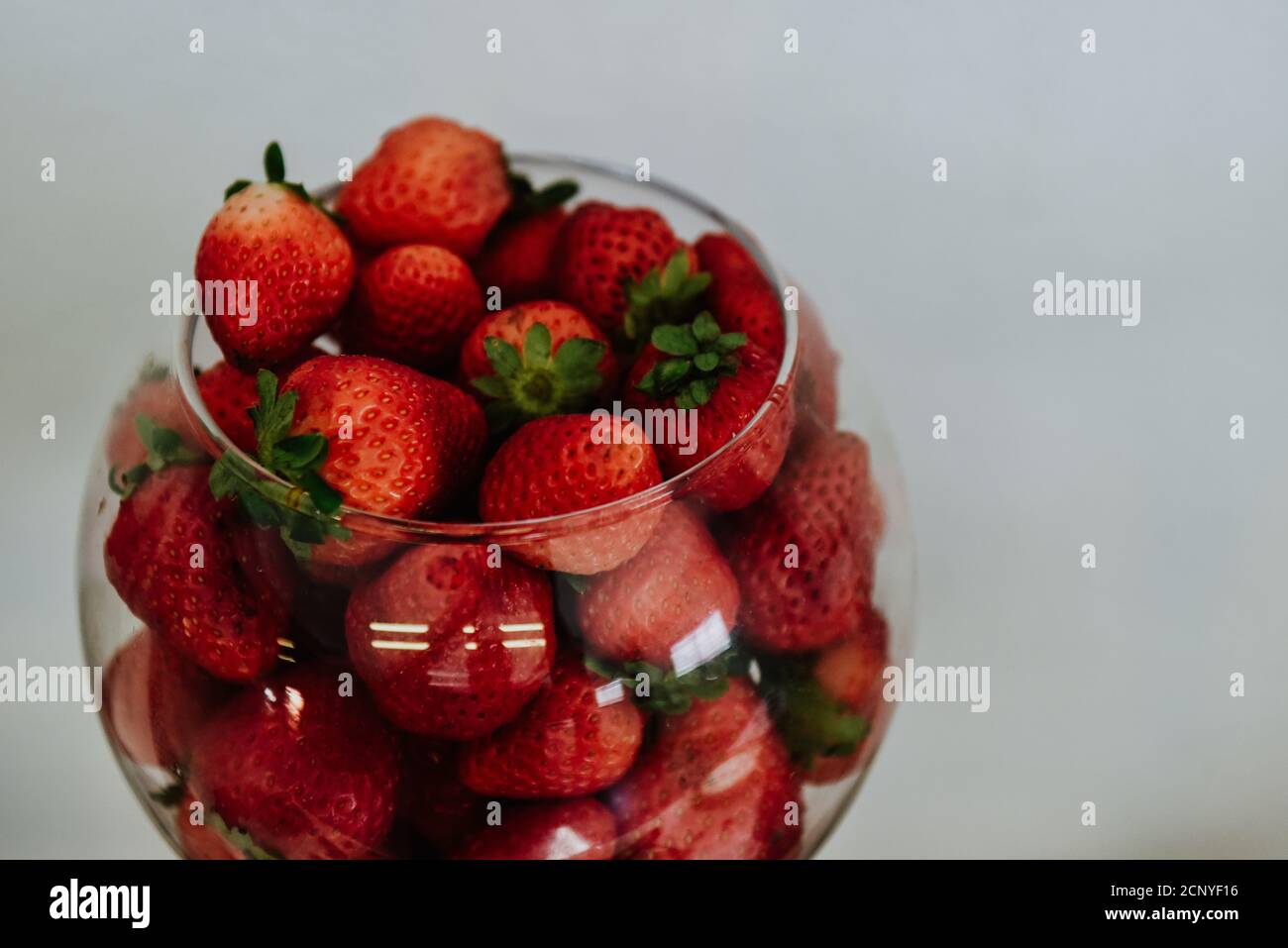 Top view closeup of a fishbowl full of strawberries on a white ...