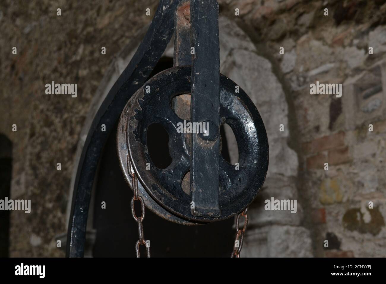 Old hand-made iron pulley with background of the walls of an ancient ...