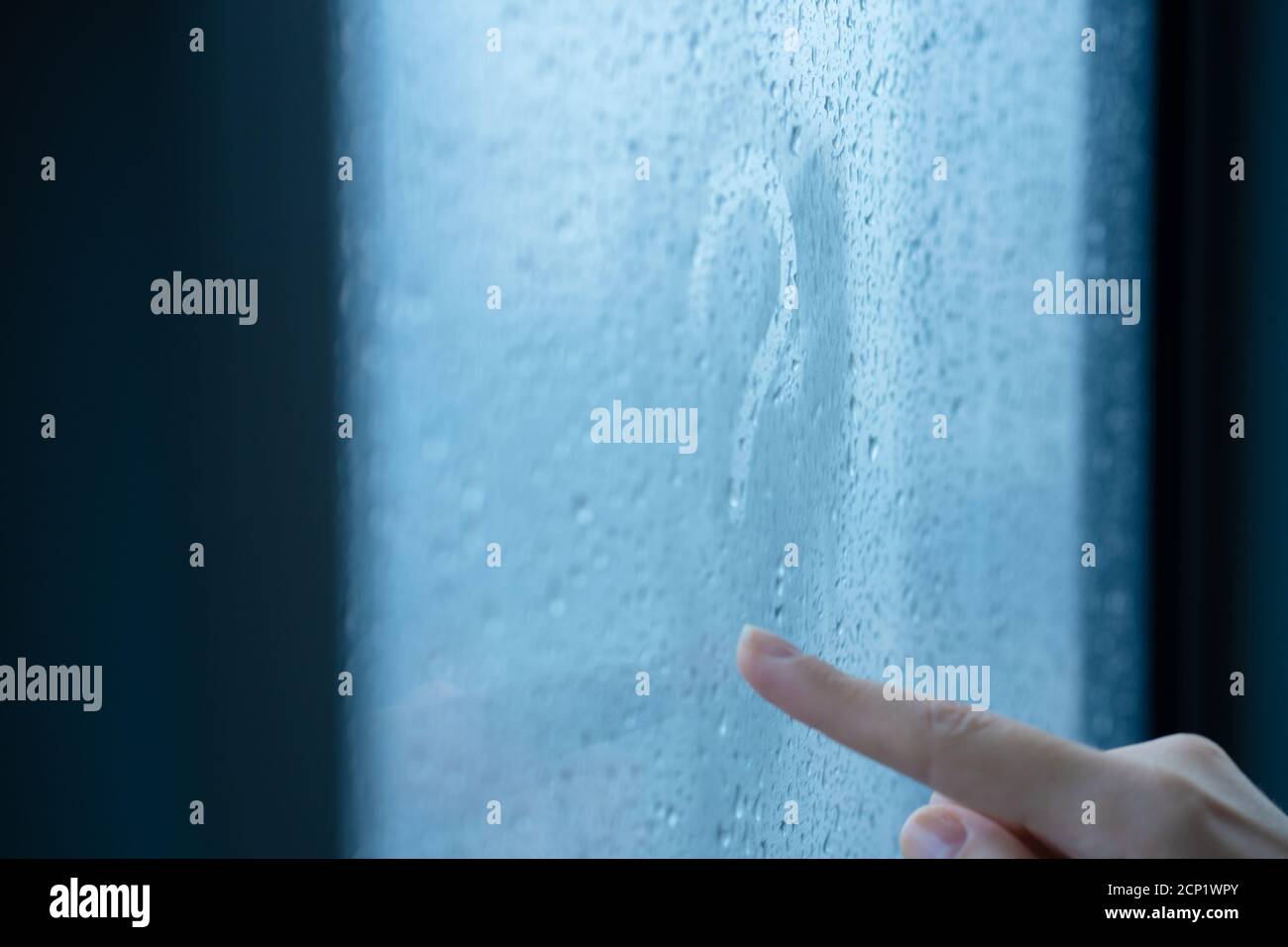 Female hand draws a question mark on a foggy window during the rain. A ...