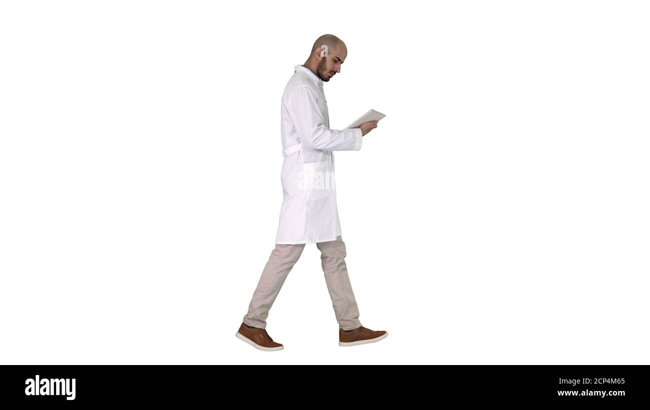Doctor checking his tablet walking on white background Stock Photo - Alamy