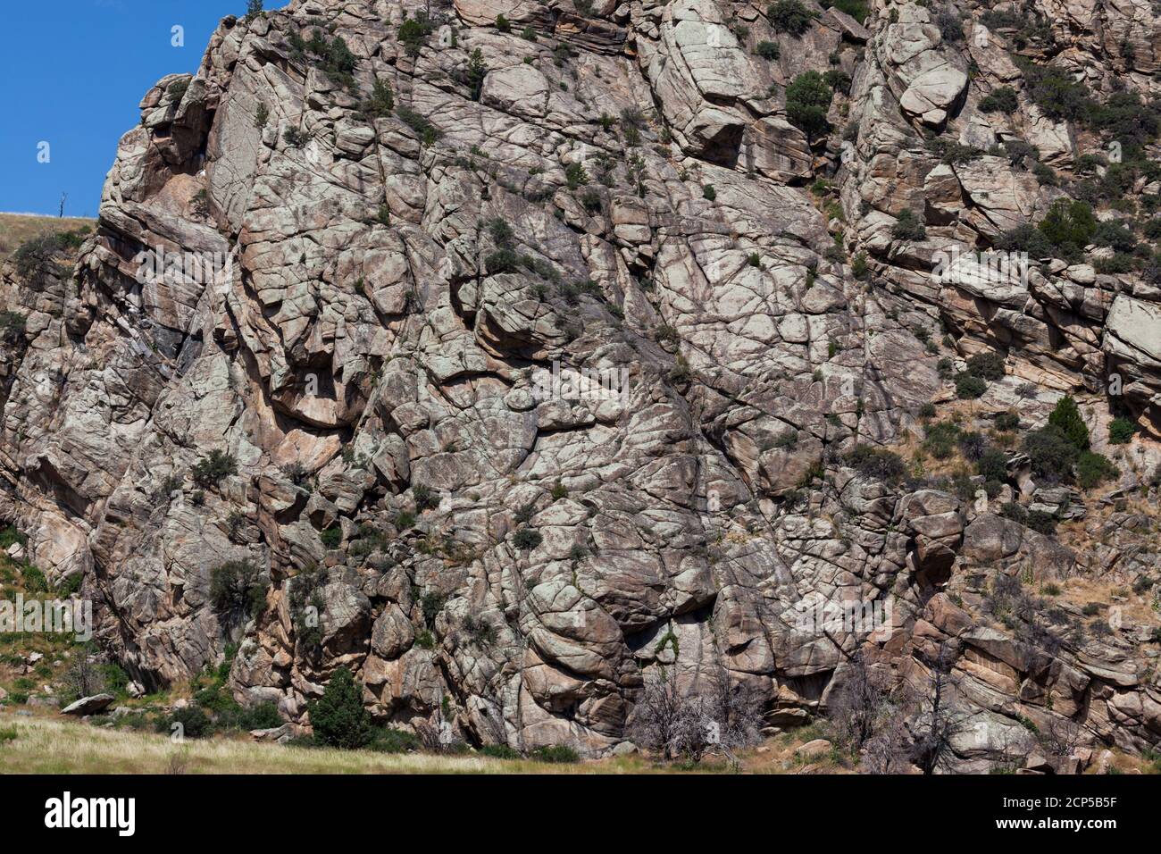 A natural rock wall with cracks and erosion lit by the summer sun to ...