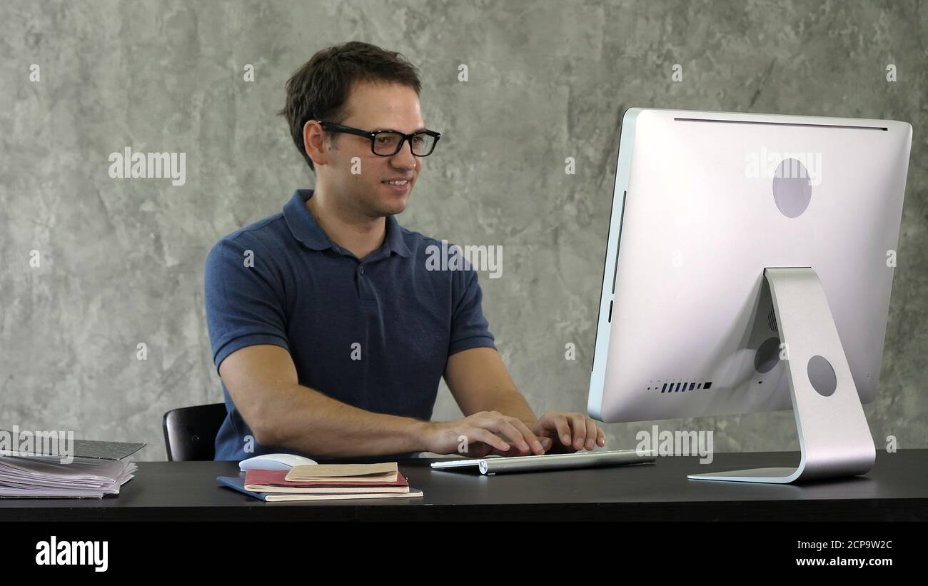 Young smiling man sitting at his desk in the office and working Stock ...