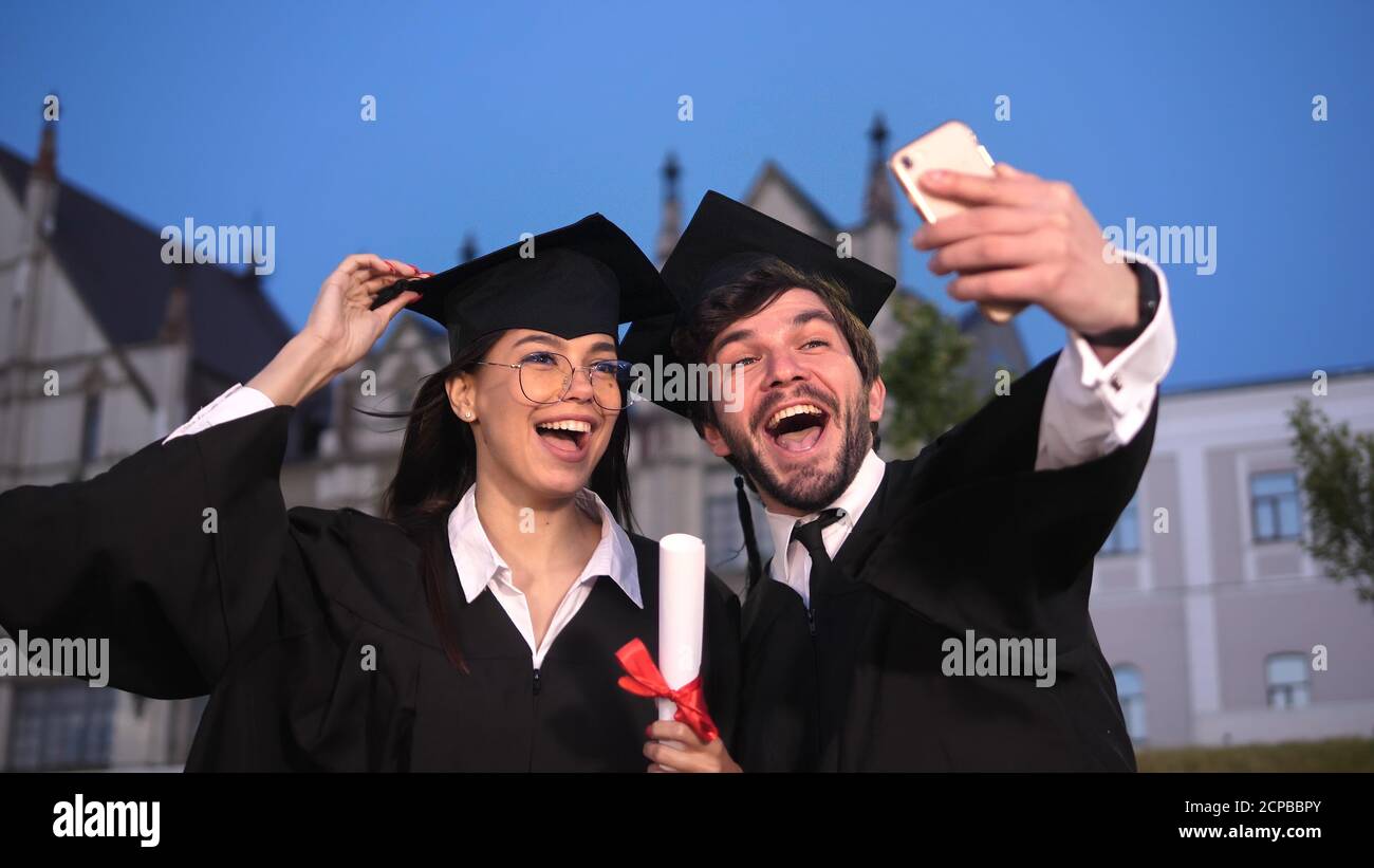 Male and female graduate students taking a selfie with mobile phone ...