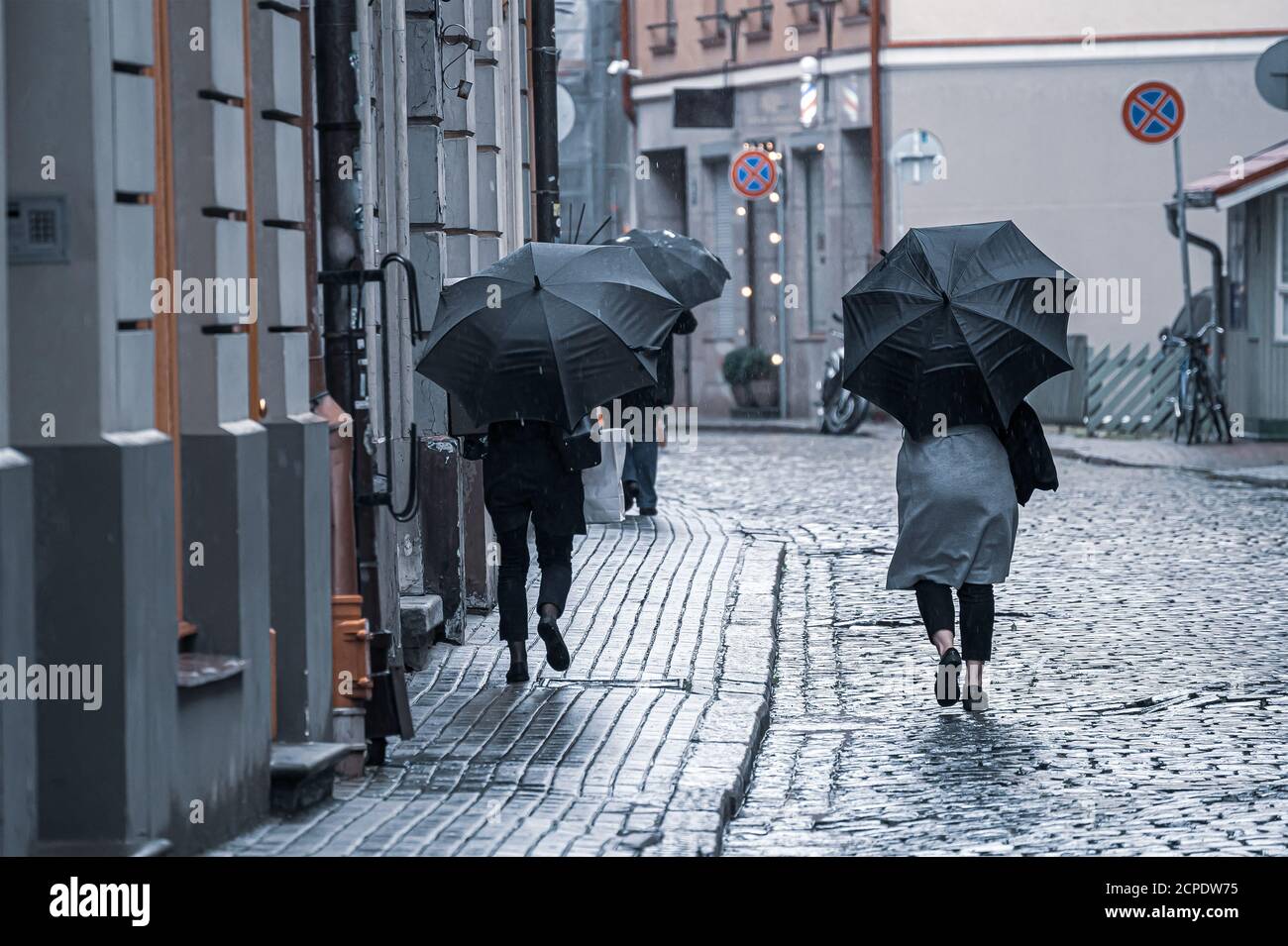 People walk down the street, hiding under umbrellas from the light rain ...