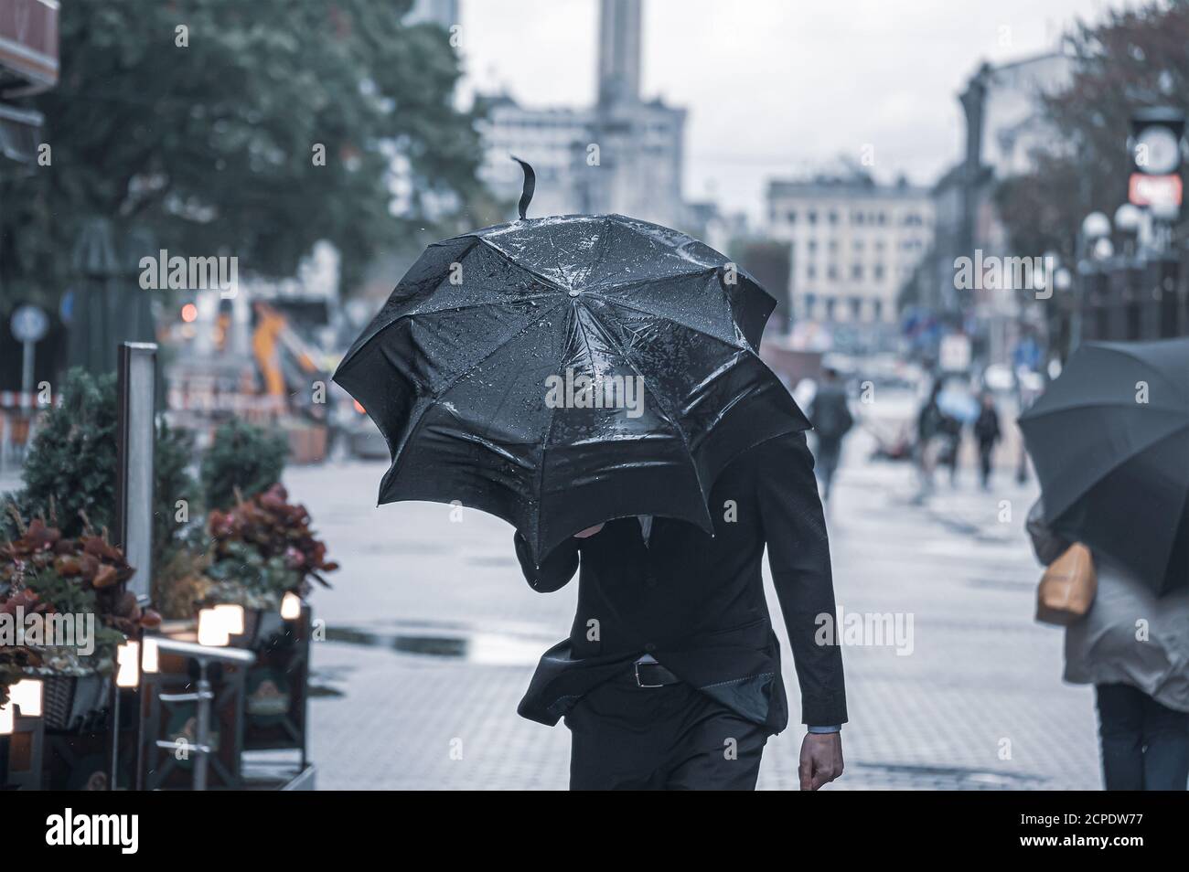 A businessman in a suit shelters an umbrella from the rain and wind ...