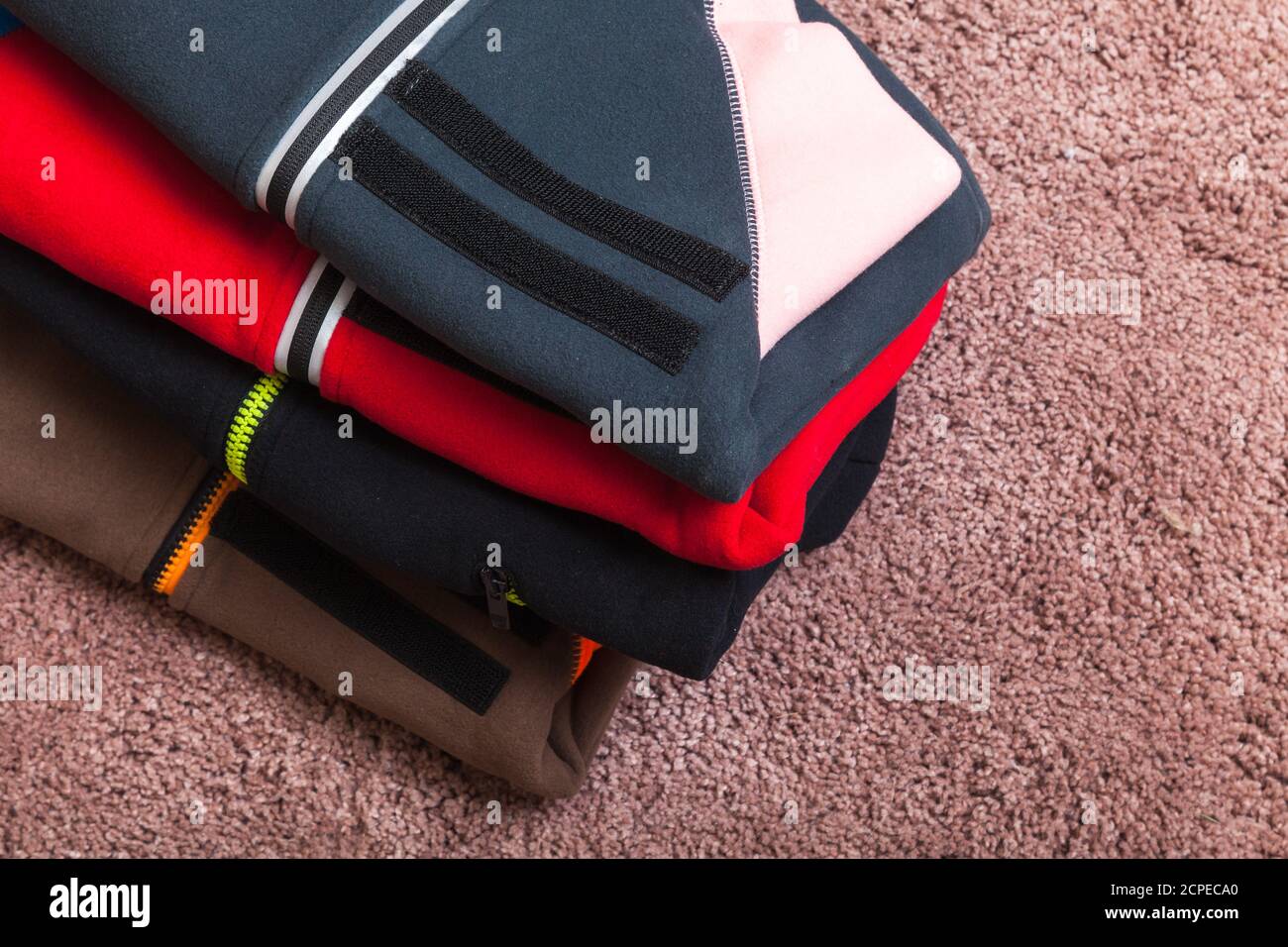 Colorful fleece jackets lay stacked on a floor carpet Stock Photo - Alamy
