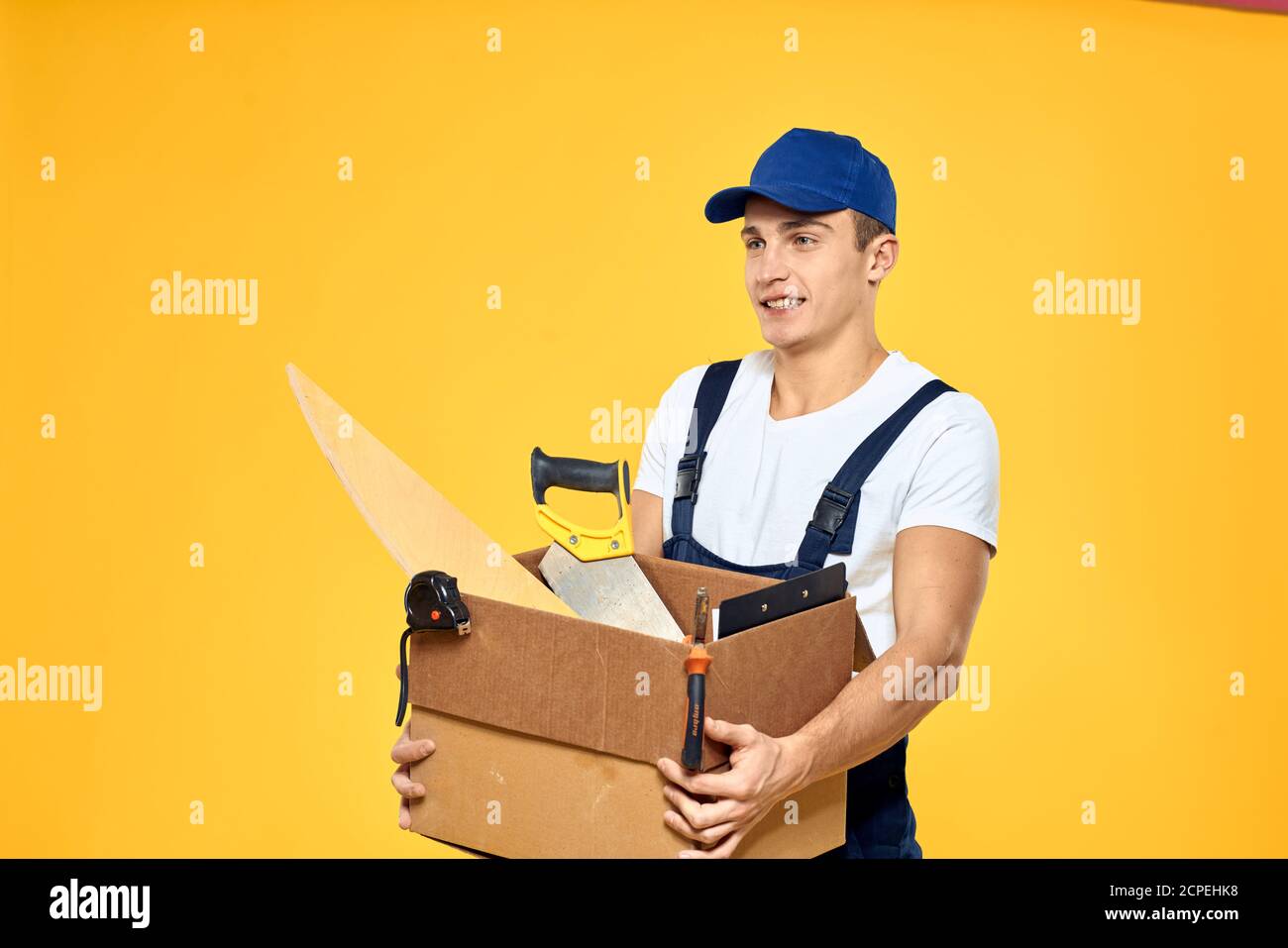 worker with box in hand tools loader yellow background Stock Photo - Alamy