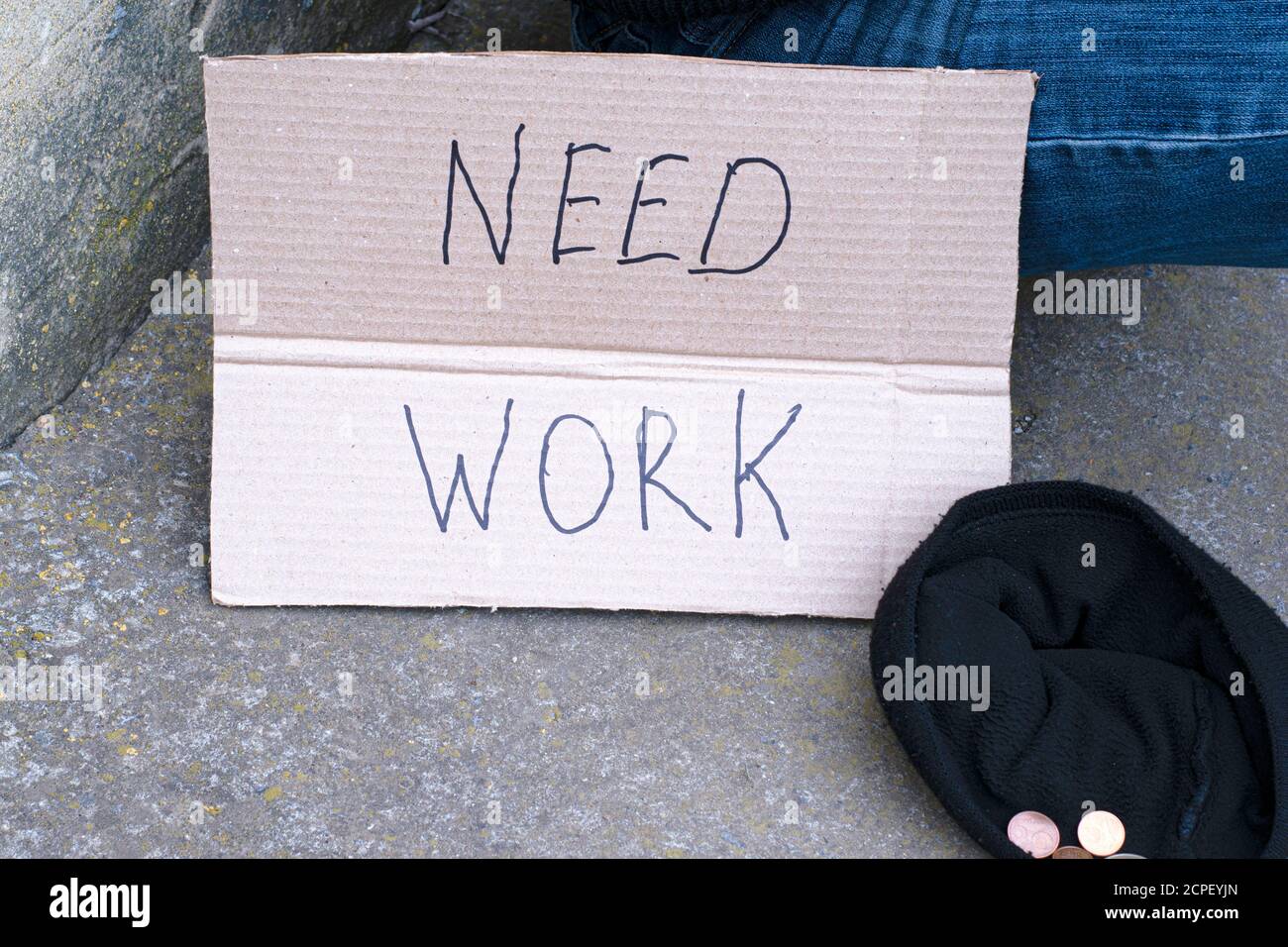 unemployed man sitting on the ground holding a cardboard sign saying ...