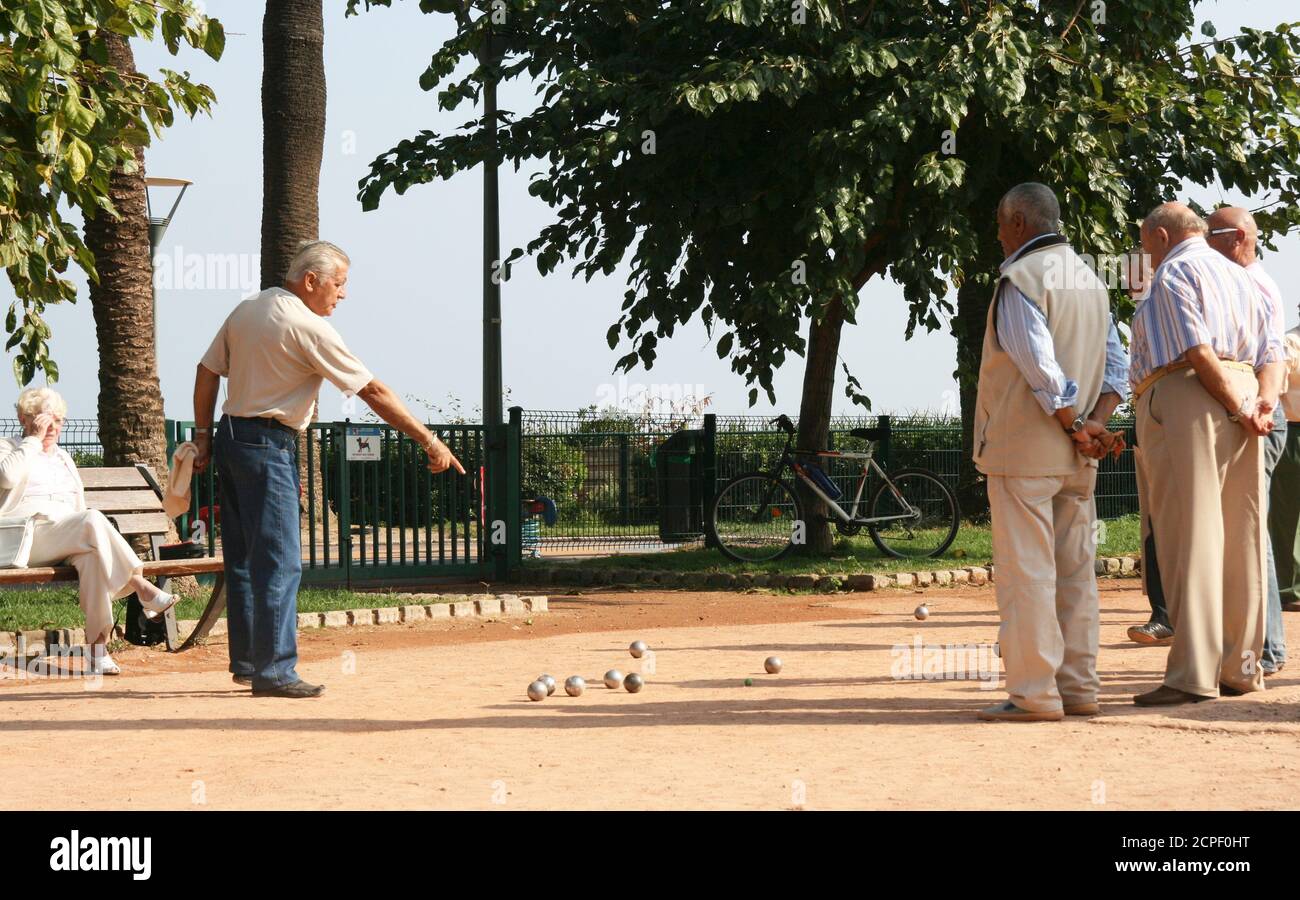 Petanque game on the promenade. The player points to the target. The ...
