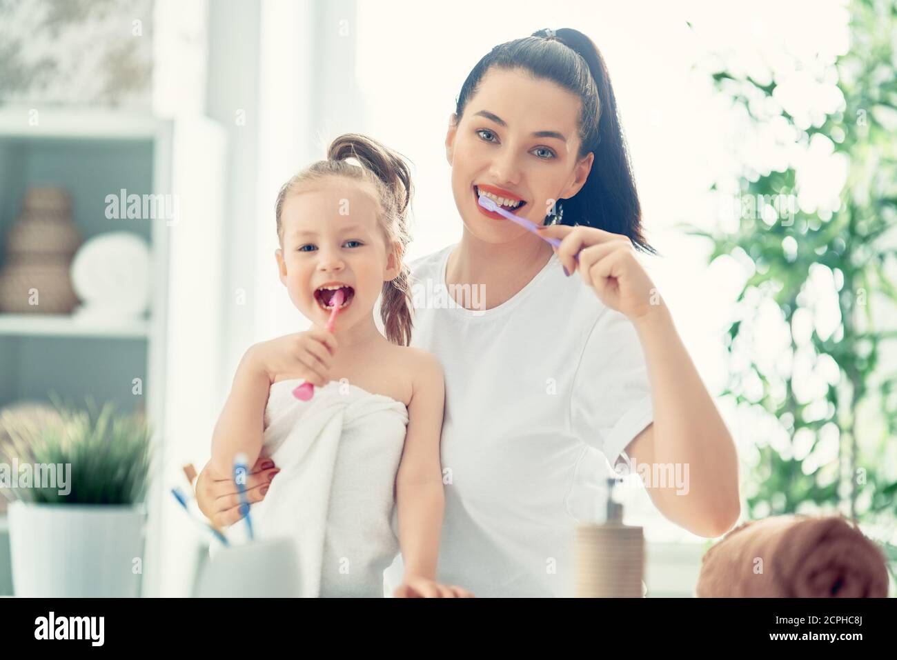 Happy family! Mother and daughter child girl are brushing teeth ...