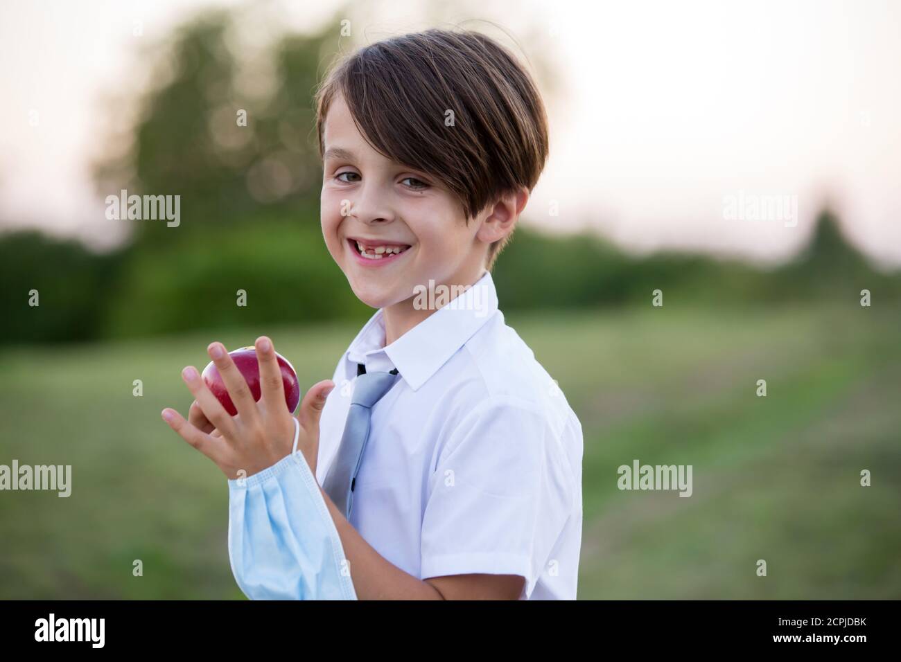 School child, boy, eating apple and holding medical mask. going back to ...