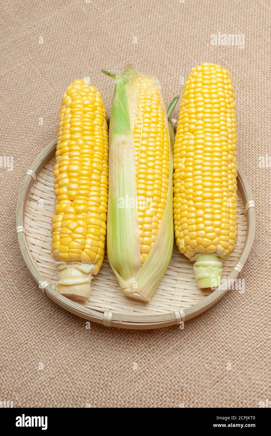 Raw corn cobs in a woven bamboo basket. Isolated on jute background ...