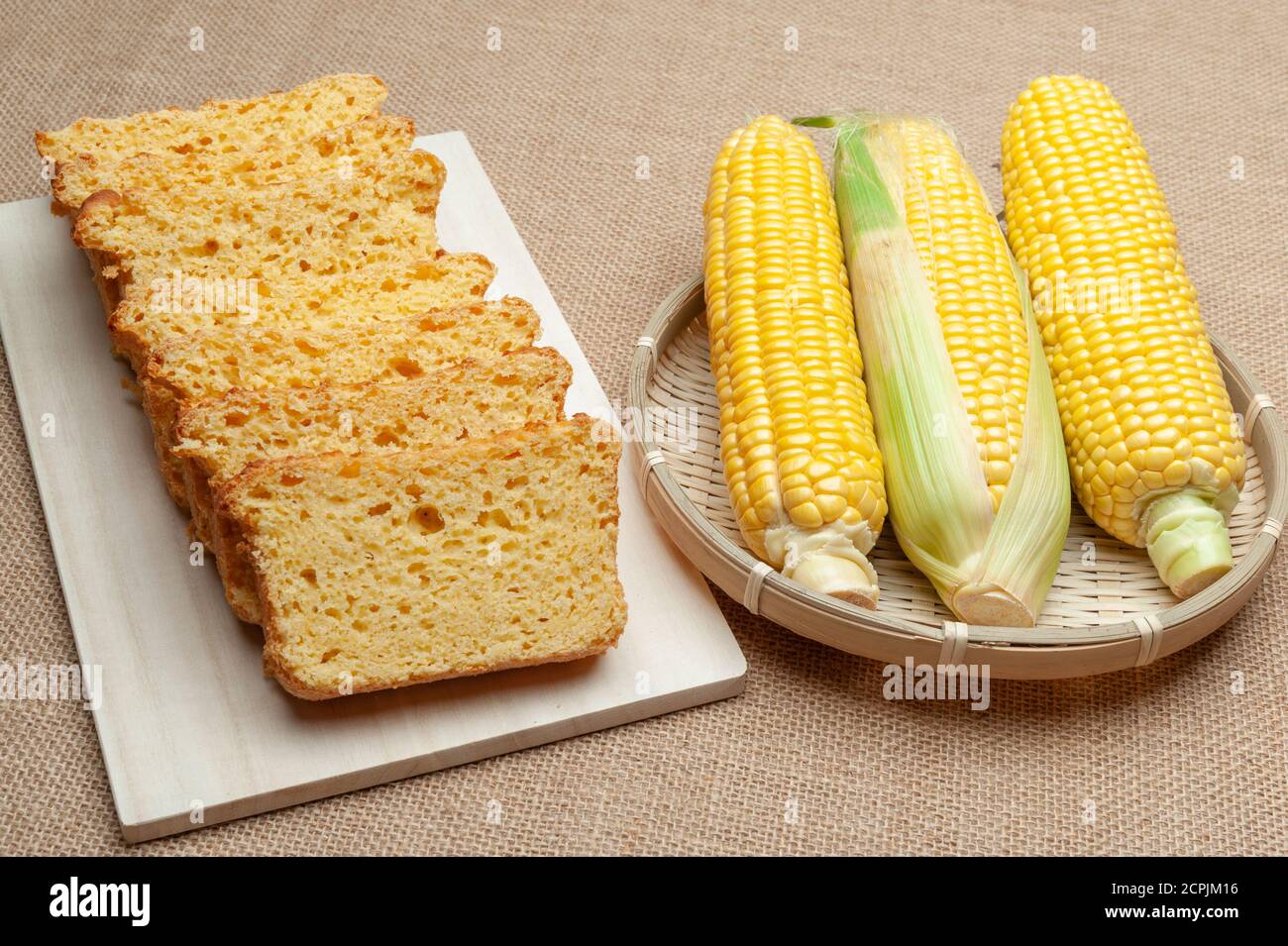 Homemade Brazilian corn bread sliced on a cutting board and raw corn ...