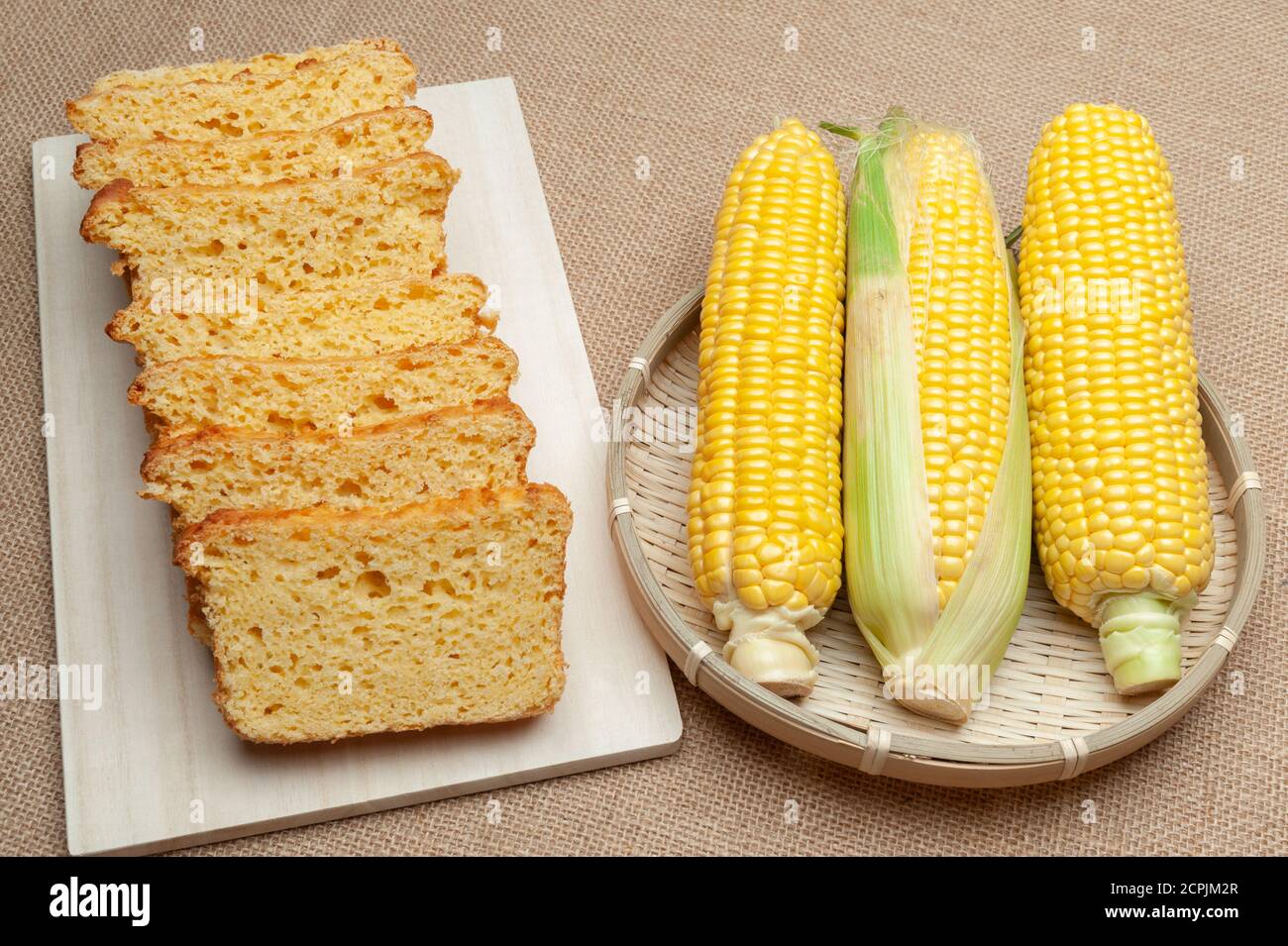 Homemade Brazilian corn bread sliced on a cutting board and raw corn ...
