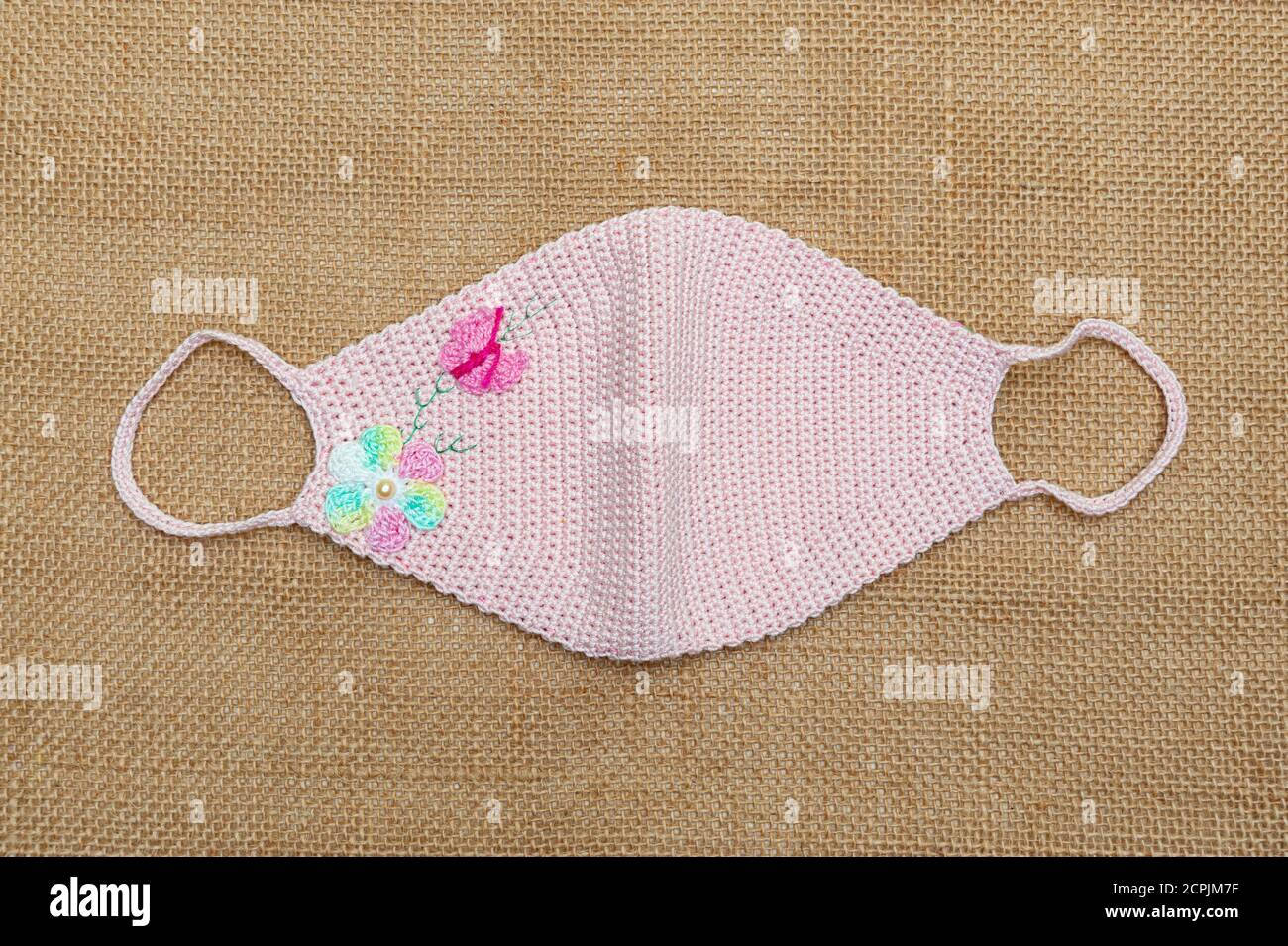 Homemade crochet face mask. Pink color with flower designs. Isolated on ...