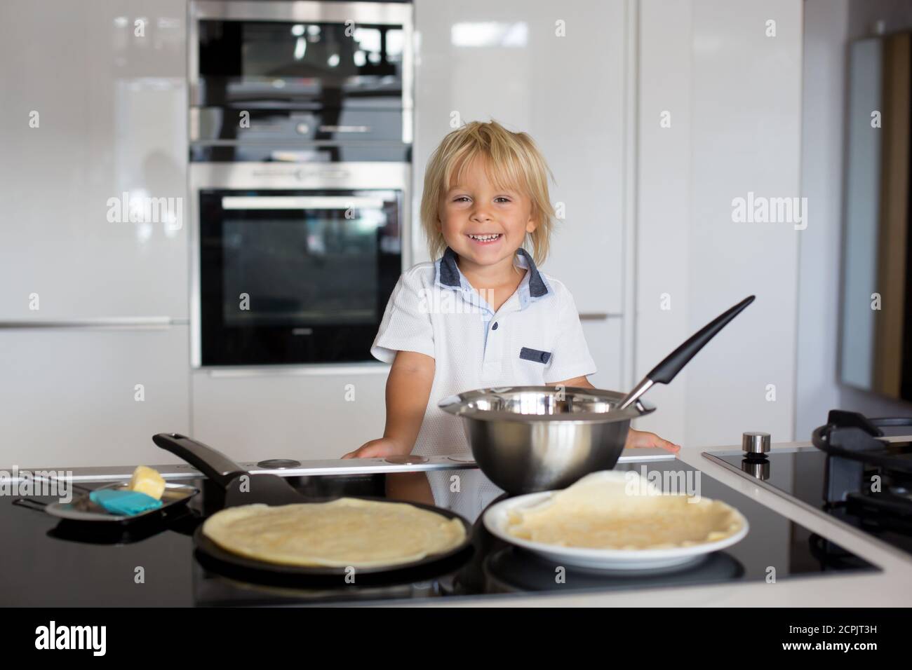 Cute toddler child, blond boy, making pancake in kitchen, eating them ...