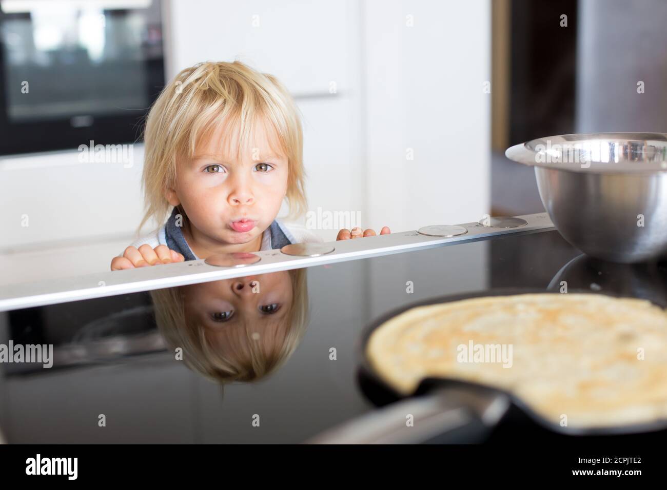 Cute toddler child, blond boy, making pancake in kitchen, eating them ...