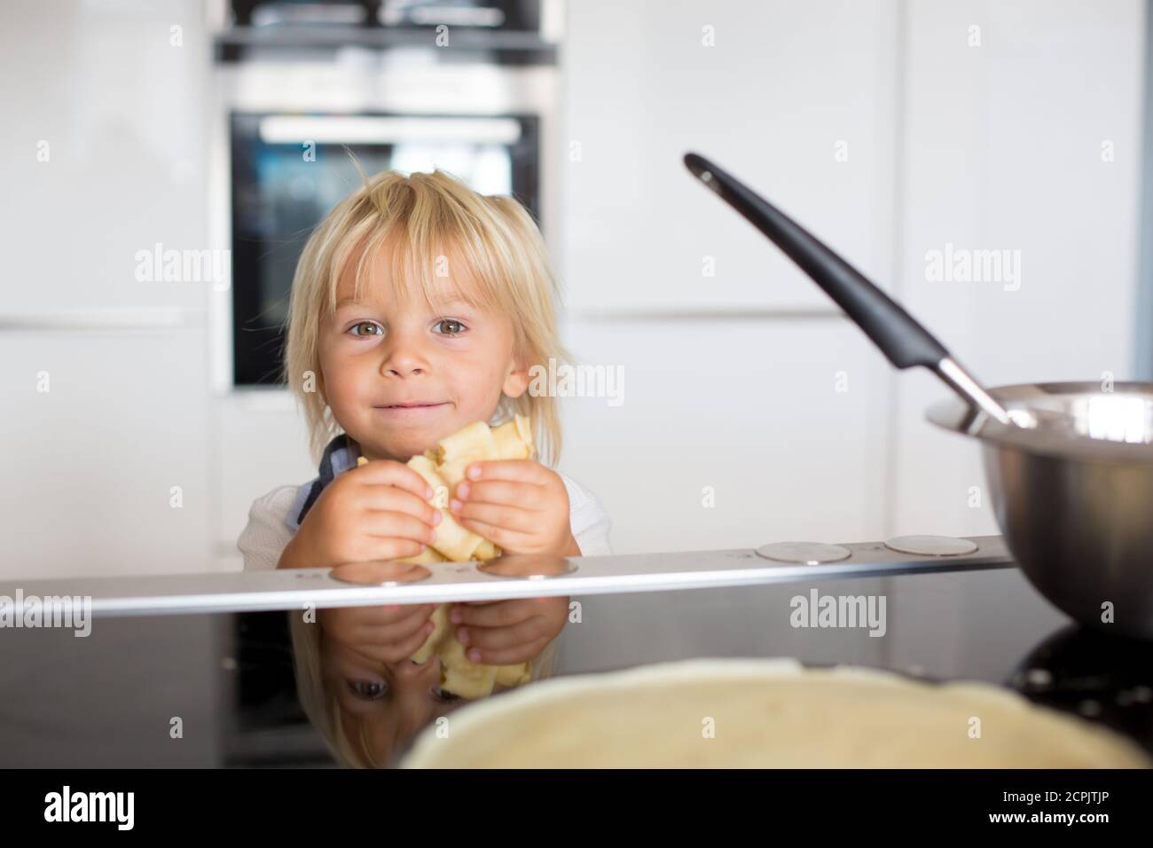 Cute toddler child, blond boy, making pancake in kitchen, eating them ...