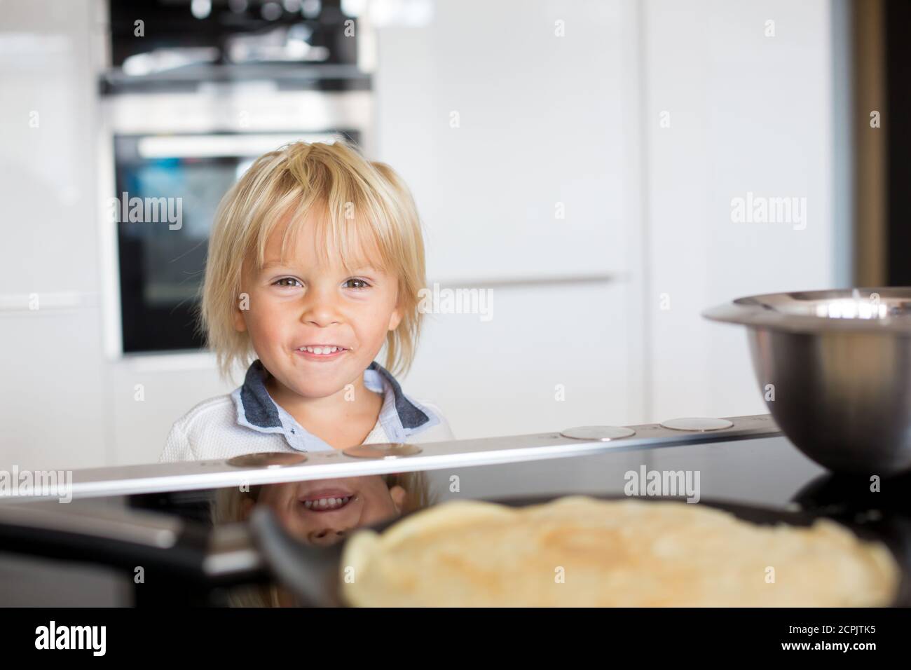 Cute toddler child, blond boy, making pancake in kitchen, eating them ...
