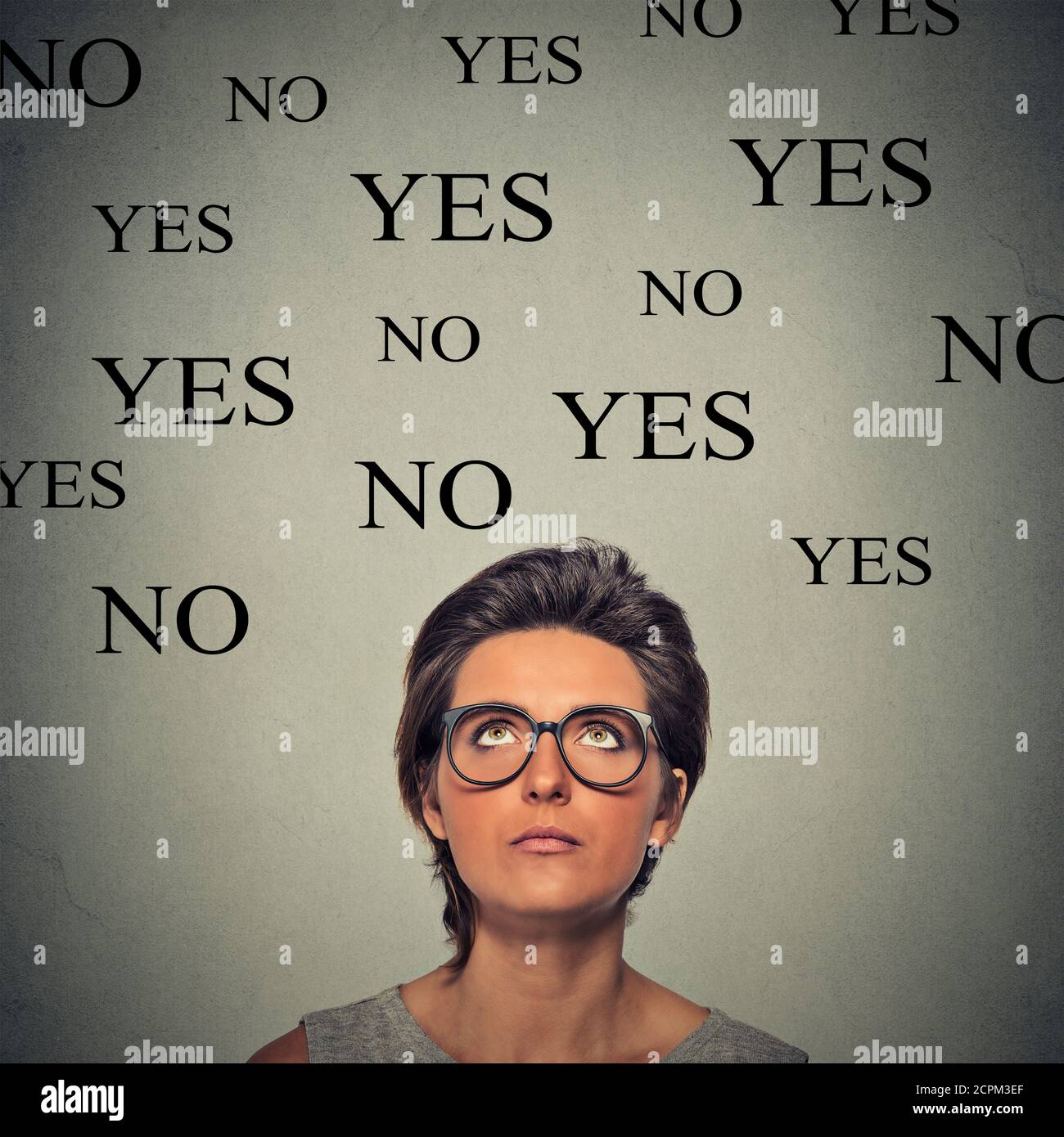 Thinking young woman with yes or no choice looking up on gray wall ...