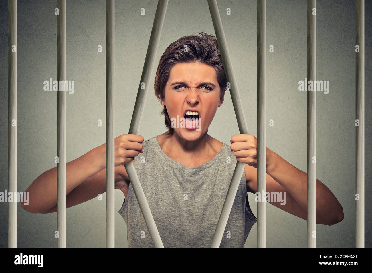 Stressed desperate angry woman bending bars of her prison cell on gray ...