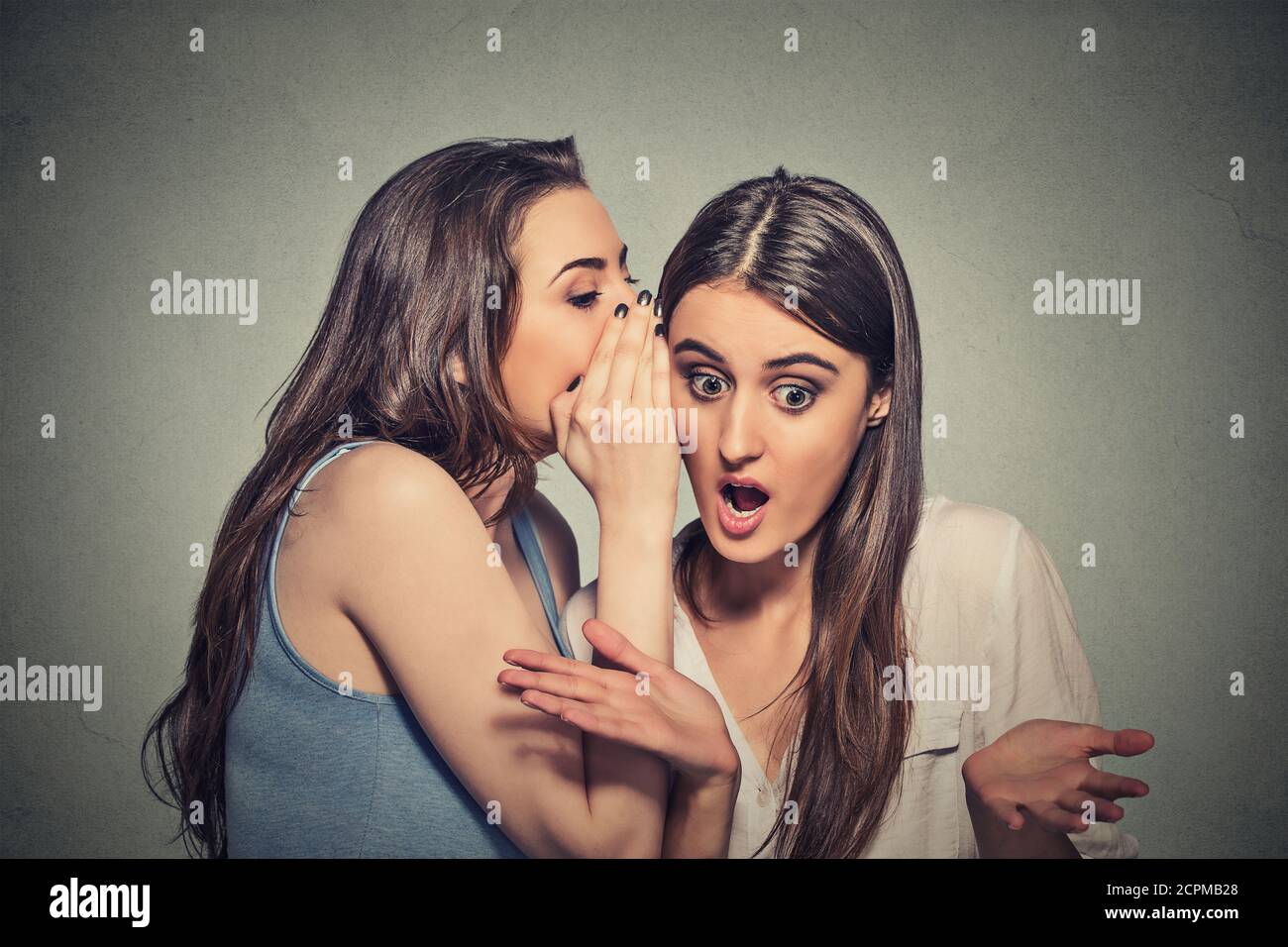 Girl whispering into woman ear telling her something funny and shocking ...