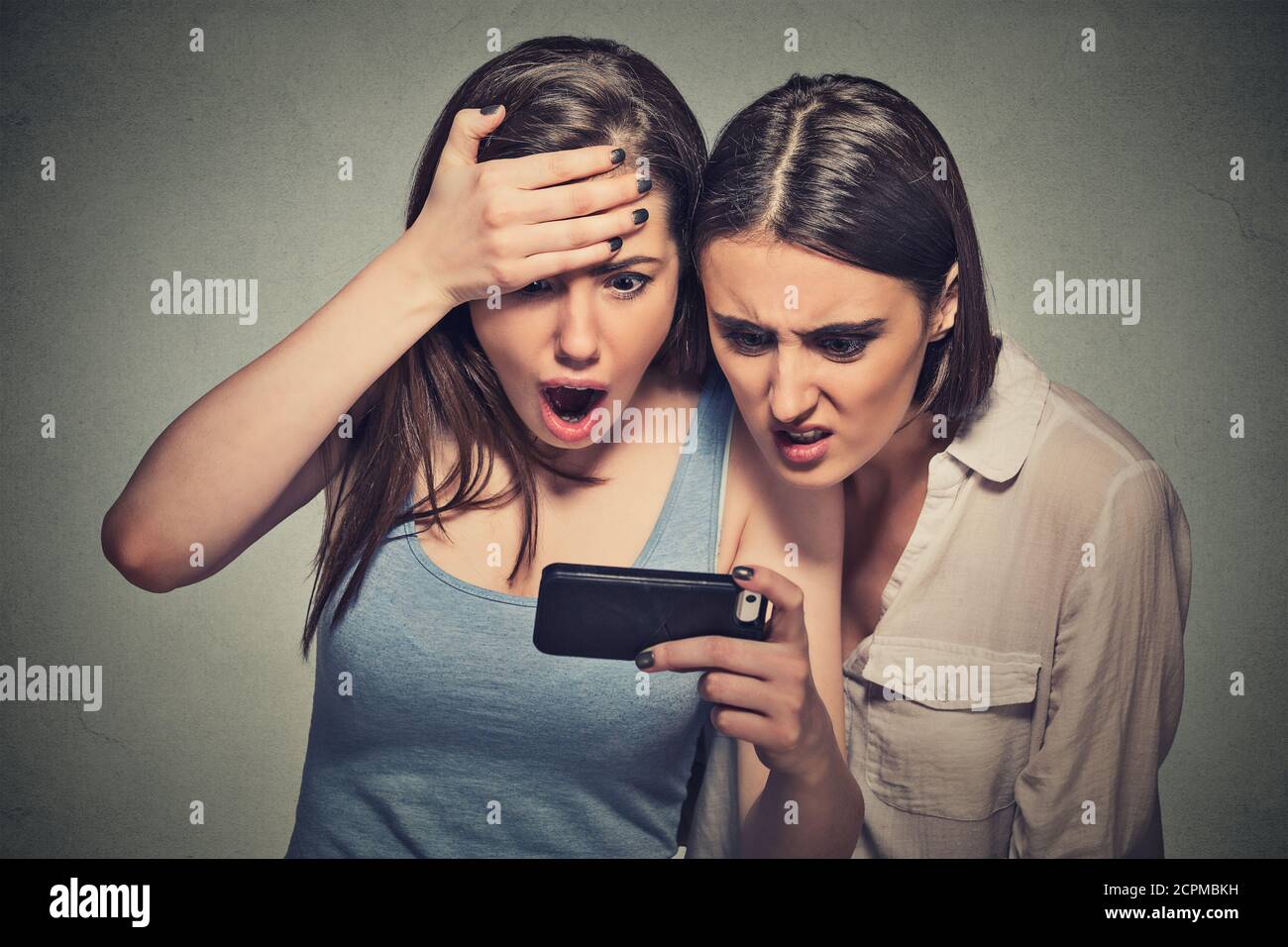 Two shocked women displeased young girls looking at mobile phone seeing ...