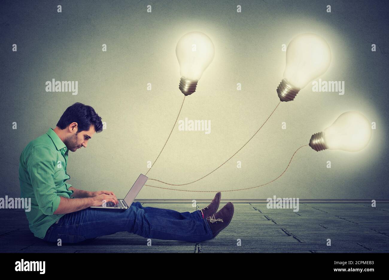 Side profile man sitting on floor using a laptop with many light bulbs ...