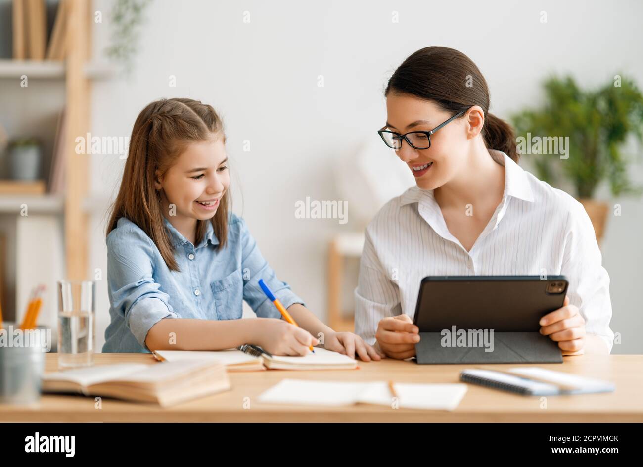 Back to school. Happy child and adult are sitting at desk. Girl doing ...