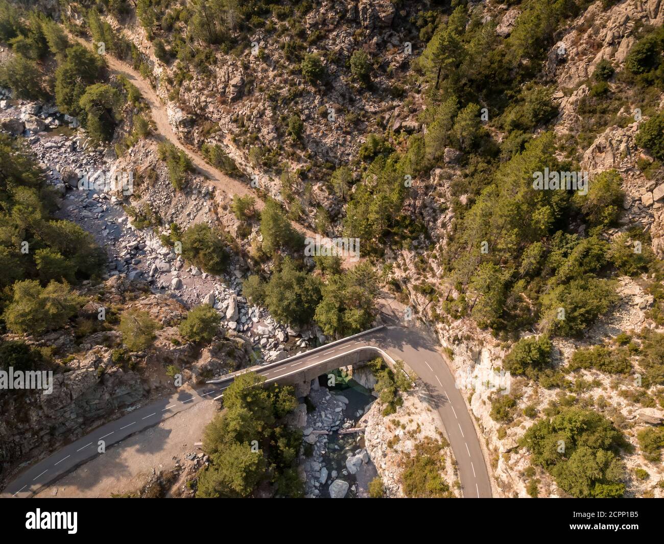 Winding road and narrow stone bridge passing over a clear mountain ...