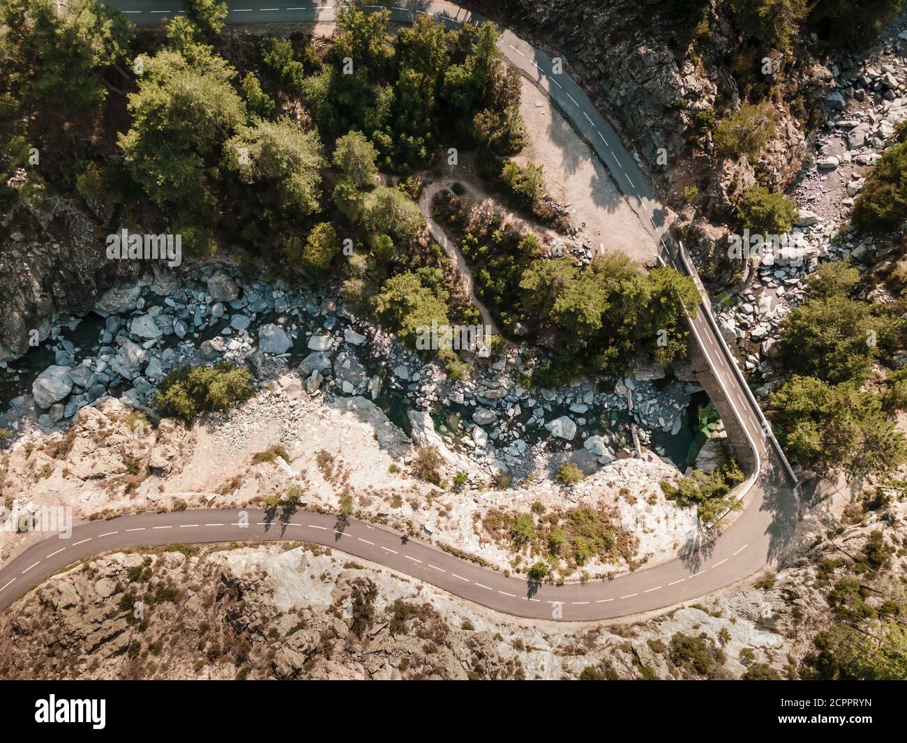 Winding road and narrow stone bridge passing over a clear mountain ...