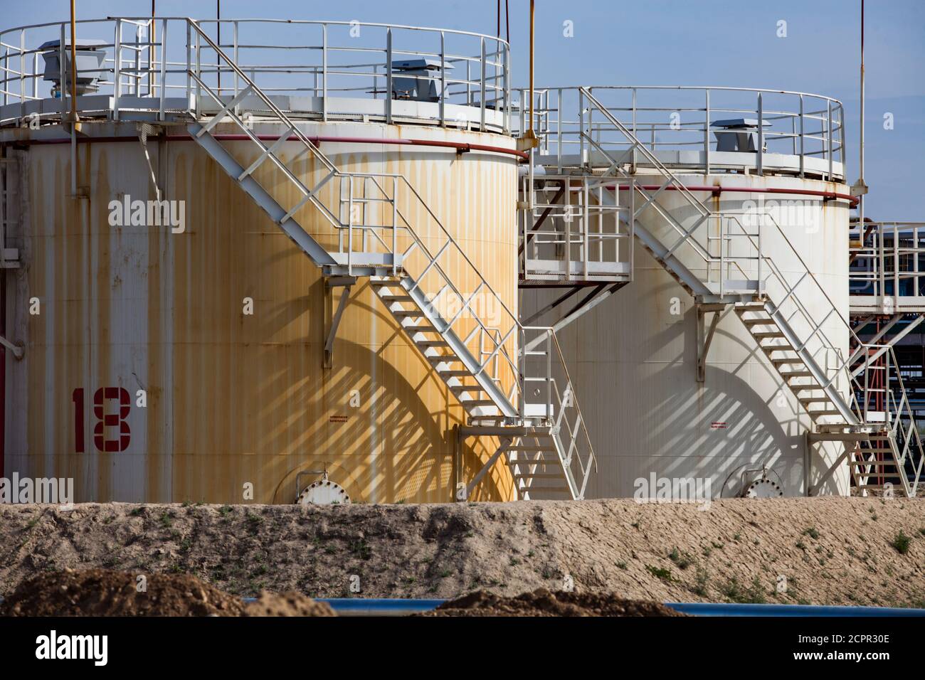 White and yellow oil storage tanks on bright sun on blue sky. Close up ...