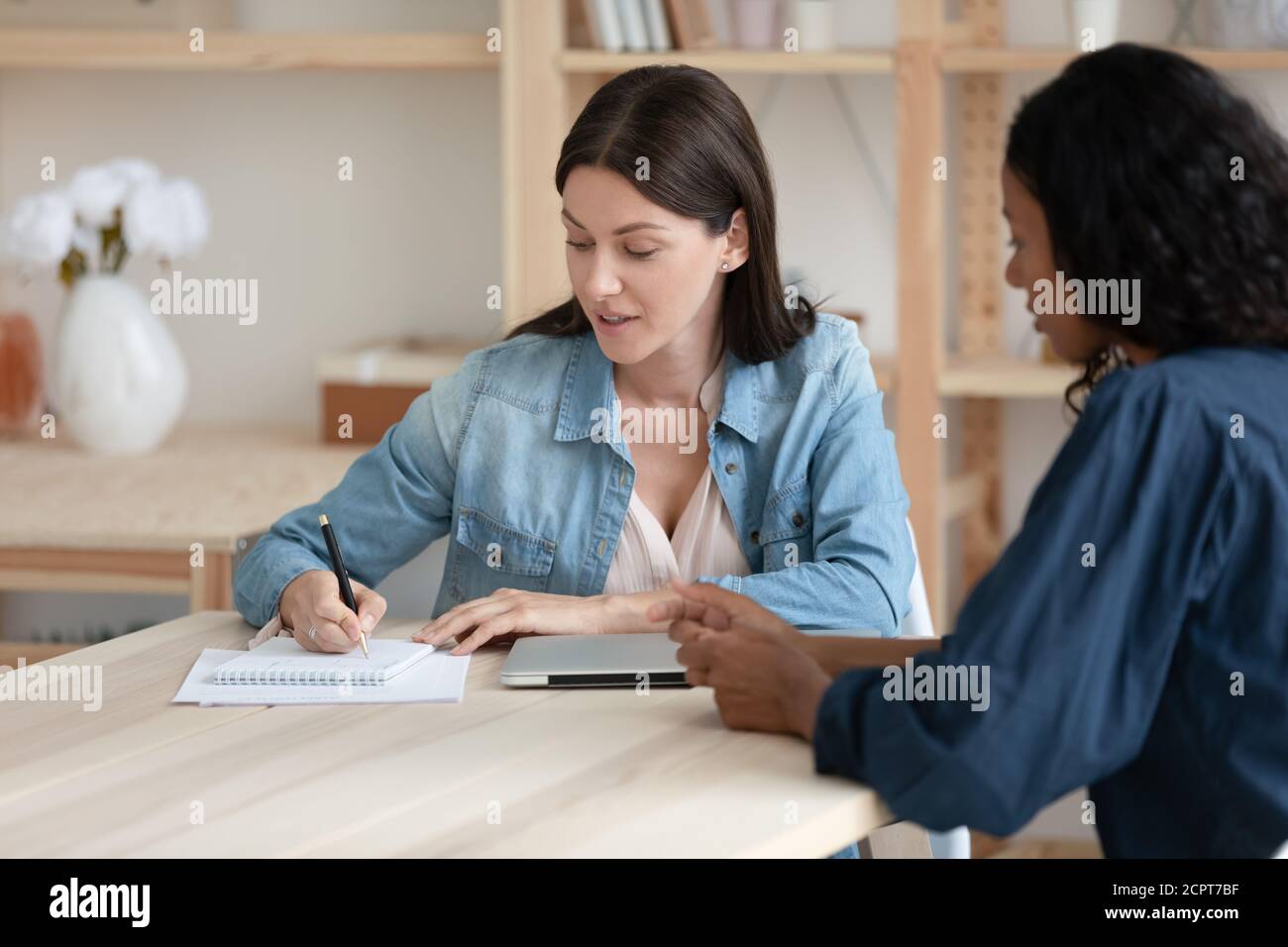 Confident businesswoman making notes at meeting, consulting African ...
