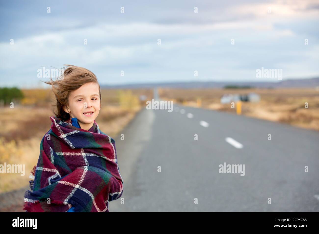 Beautiful child, standing on a road on a very windy day, wrapped in ...