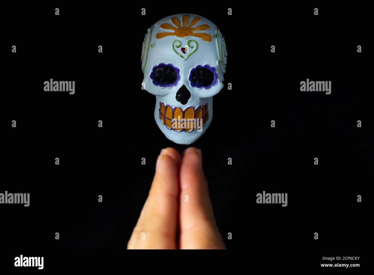 Hands of a man praying to a skull head of the day of the dead painted ...