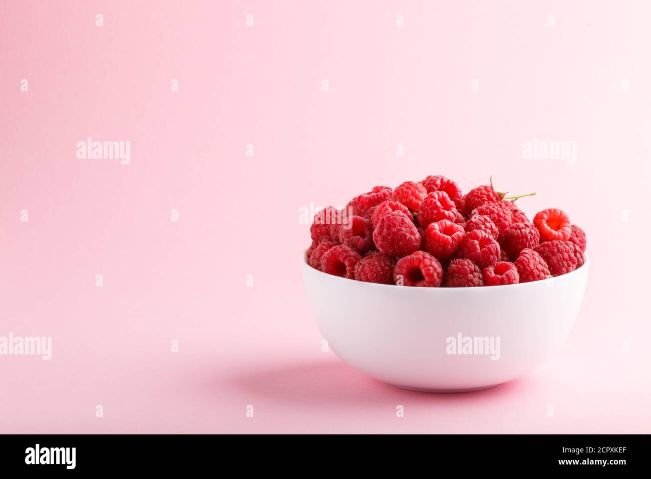Fresh raspberry in white bowl on pink pastel background. side view ...
