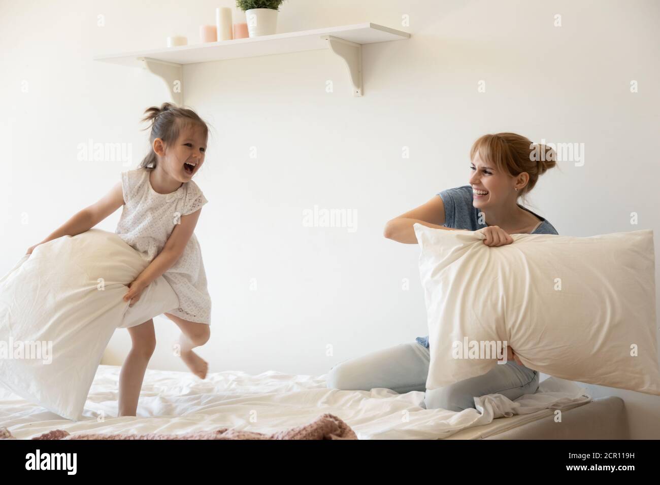 Cheerful mum and daughter fighting with pillows at home Stock Photo - Alamy