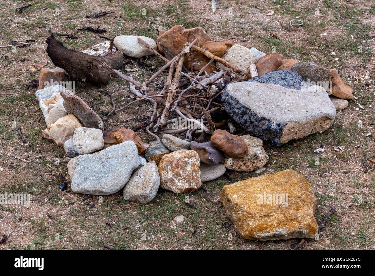 a camp fire surrounded by stones on a beach with driftwood and sticks ...
