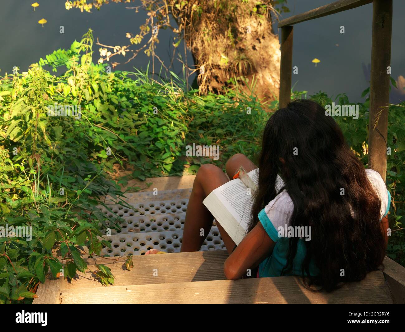 Métis girl seen from behind reading a book on a staircase outside at ...
