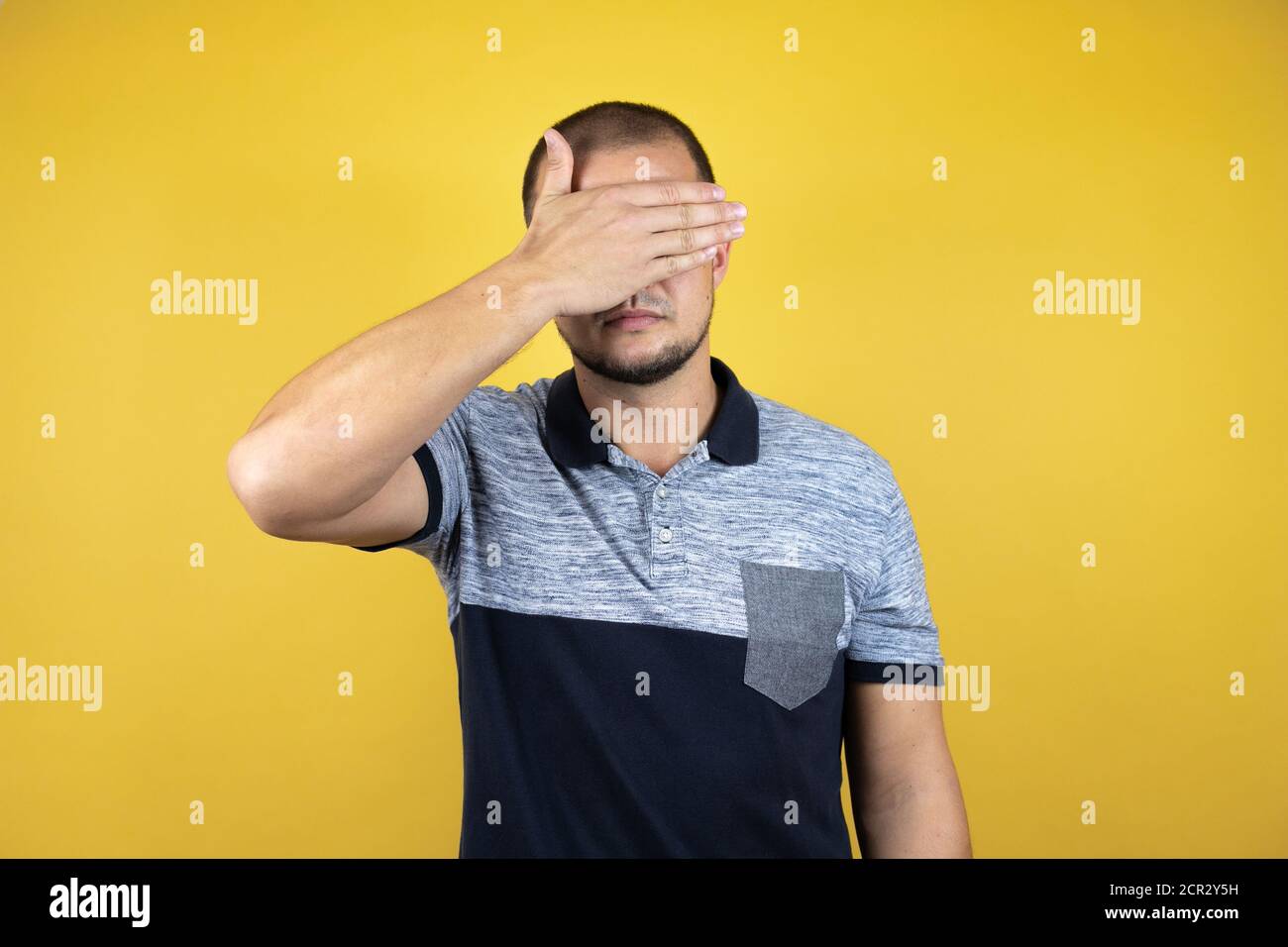 Russian man standing over insolated yellow background covering eyes ...