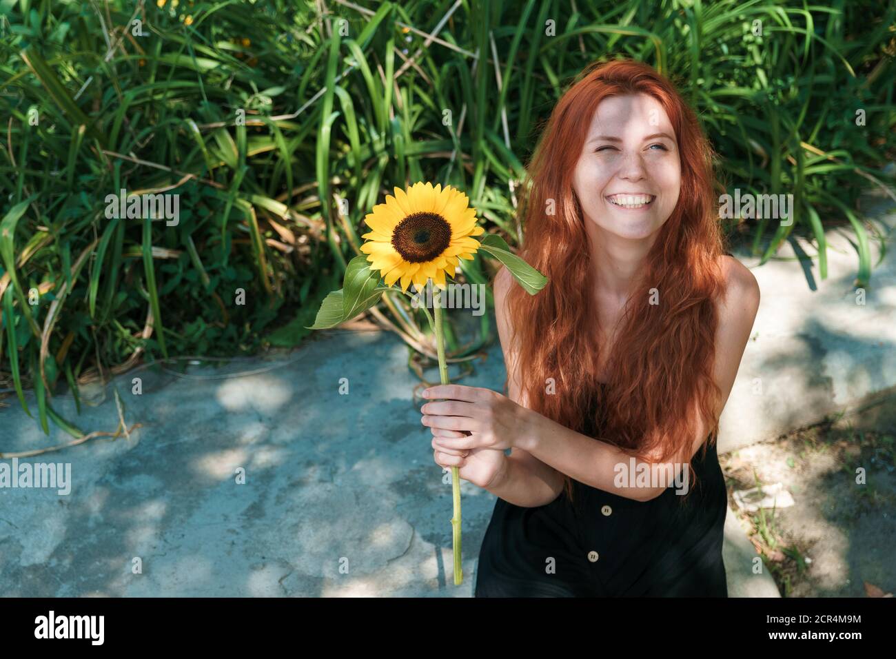 Ginger girl with sunflower in shade of tree looks at sun. Spring mood ...