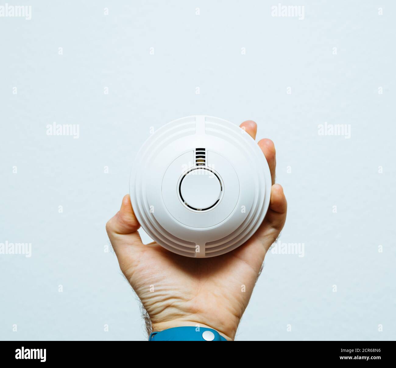 Male hand holding smoke fire alarm in hand against white background ...
