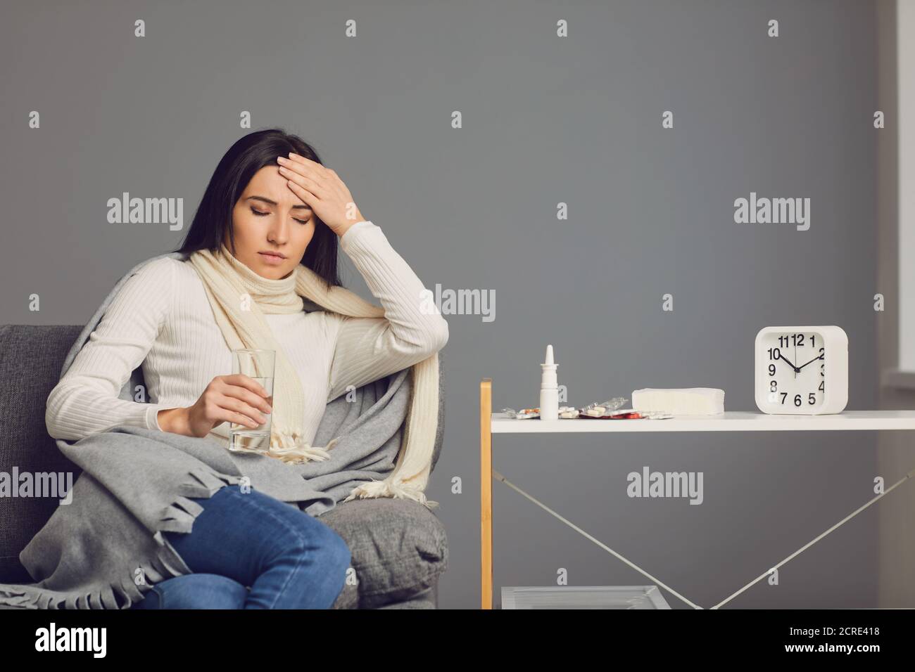 A sick girl with a fever looks at a thermometer while sitting on a sofa ...