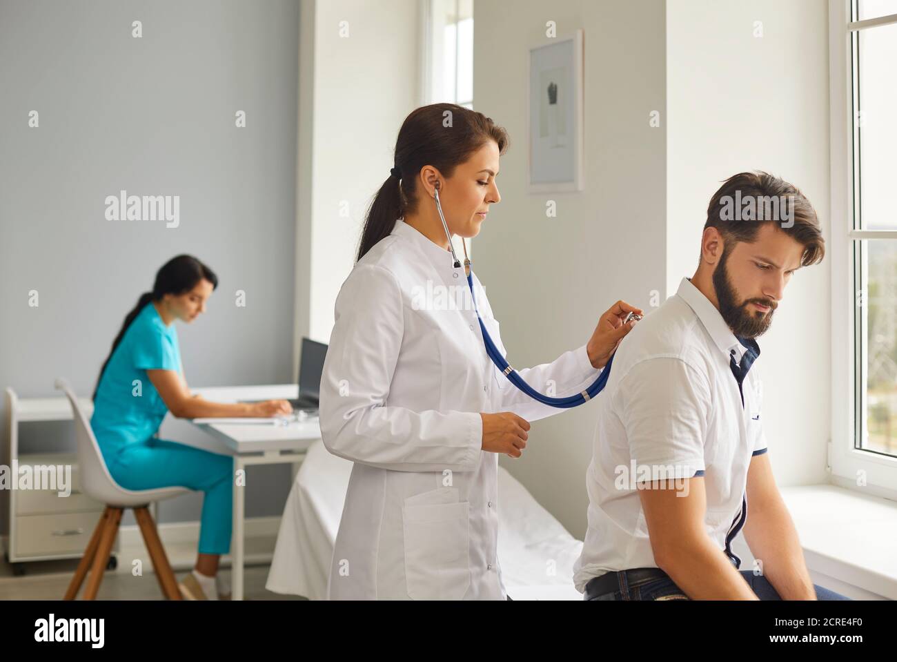 Female doctor listens to breathing with a stethoscope in a young ...