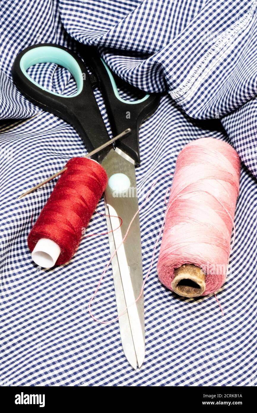 two spools of thread, a needle and scissors on a piece of tartan Stock ...