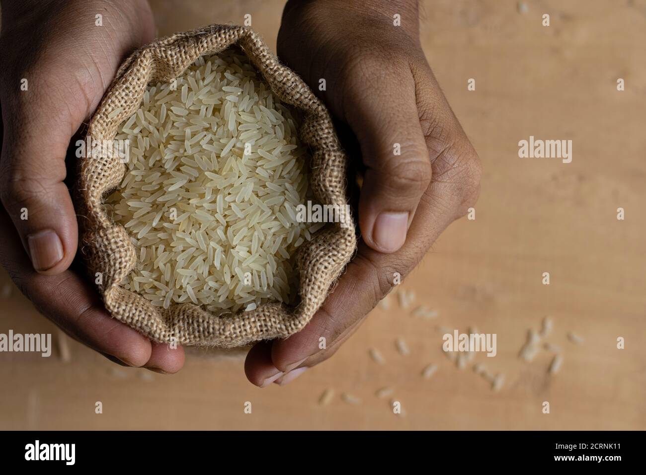 jute bag of rice held in human hand above wooden floor background Stock ...