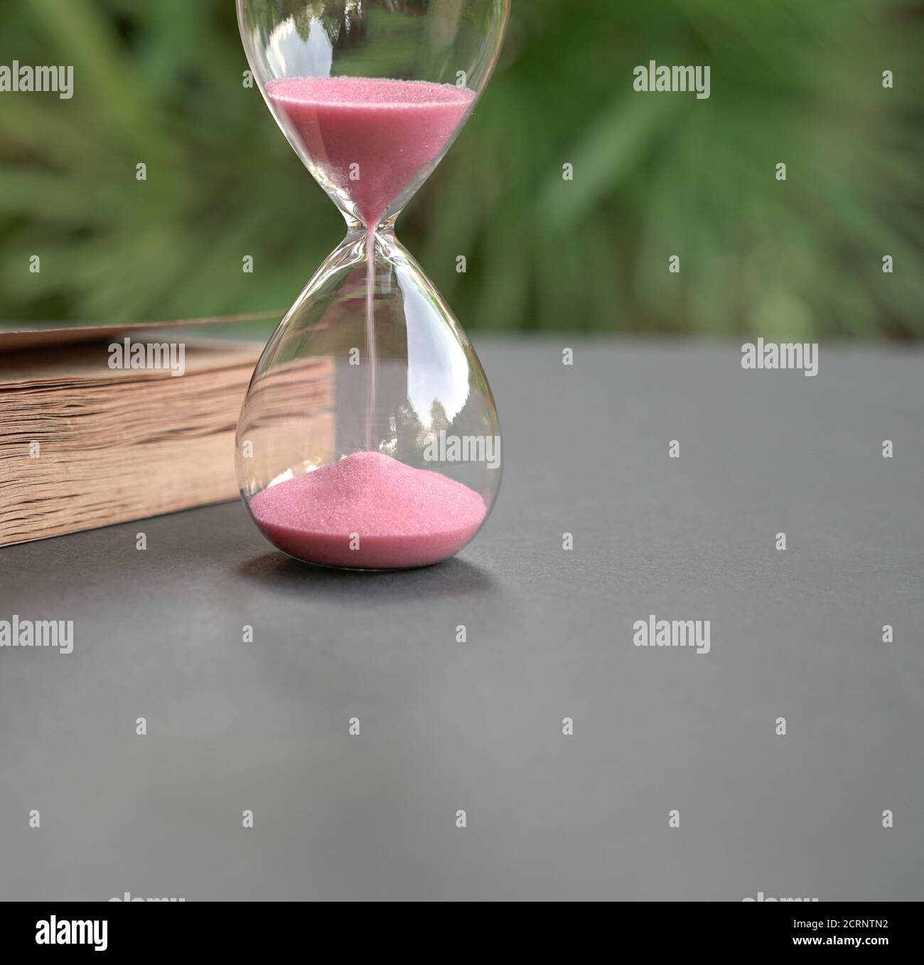 Hour glass with sand flowing, next to a book. Close up. Time management ...